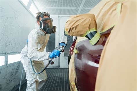 보호복과 마스크를 쓴 자동 화가는 스프레이 건을 사용하여 자동차 문에 얇은 또는 다른 청소기를 분사합니다 현지 수리를 위한 차량 차체 요소 준비 차에 대한 스톡 사진 및