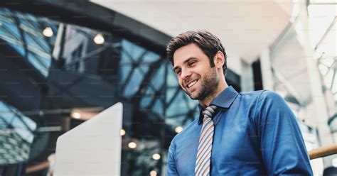 젊은 잘생긴 사업가가 노트북을 사용하여 현대적인 건물의 벤치에 앉아 있다 사진 Unsplash의 랩톱 이미지