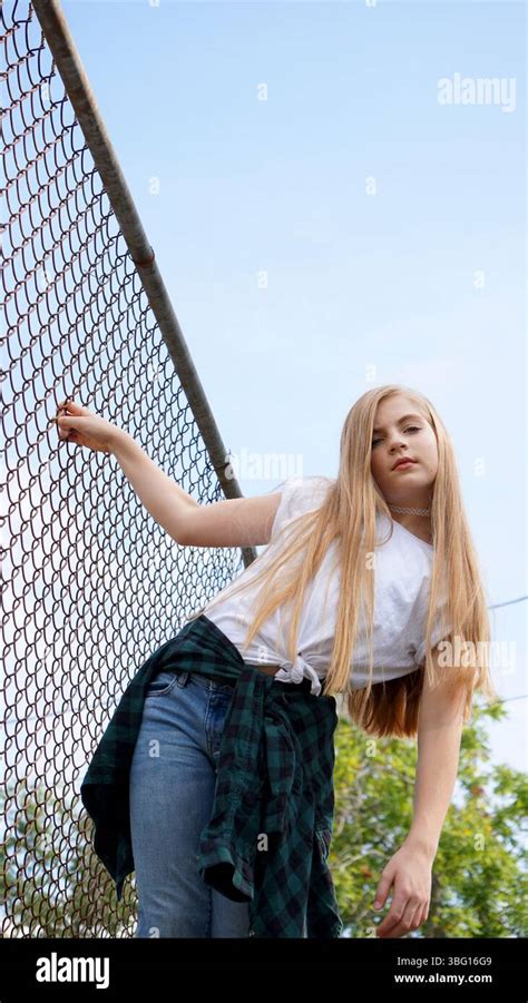 Pre Teen Girl With Long Blonde Hair Holding A Chain Link Fence On A