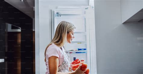 앞치마를 두르고 웃는 백인 금발 주부가 냉장고에서 야채를 꺼내고 있습니다 여자는 가족을 위해 저녁 식사를 준비하고 싶어합니다 사진 Unsplash의 냉장고 이미지