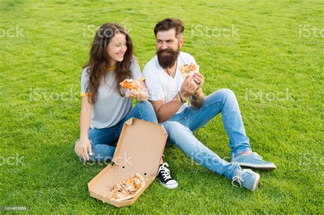 패스트 푸드 배달 수염을 가진 남자와 여자는 치즈 피자를 즐깁니다 피자와 함께 야외에서 데이트하는 것을 좋아하는 커플 배고픈 학생들이 음식을 나눕니다 순수한 즐거움 녹색