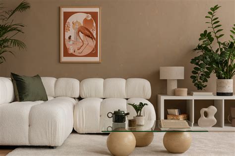 녹색 식물 모형 포스터 프레임 예술 Boucle 소파 세련된 커피 테이블 패턴 깔개 대리석 램프 및 개인 액세서리가있는 거실 인테리어의 따뜻하고 아늑한 가을 베이지 색 구성