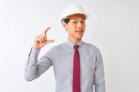 넥타이와 헬멧을 쓰고 고립된 흰색 배경 위에 서있는 중국 건축가 남자는 손가락과 카메라를 보고 작은 크기의 표지판을하고 손으로 미소와 자신감 몸짓 개념을 측정합니다 개념에