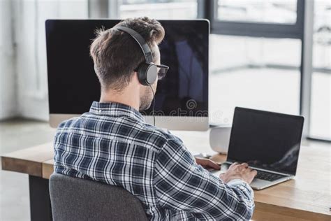 Back View Of Young Programmer In Headphones And Eyeglasses Working