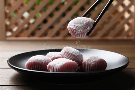 Taking Delicious Mochi From Plate With Chopsticks On Wooden Table