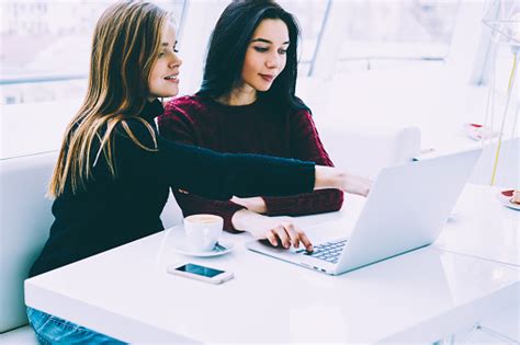 귀여운 금발 동료와 함께 시간을 보내는 동안 노트북 컴퓨터를 가리키는 긍정적 인 좋은 찾고 금발 디자이너 젊은 힙스터 여자 작업 에 현대 장치 동안 앉아 있는 동공 공간 2