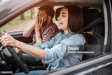 소녀는 차를 몰고 웃 고 있습니다 남자는 그녀 외에 앉아 있다 그는 여자 친구의 운전 때문에 무서 워 합니다 젊은 남자는 손으로 자신의 얼굴을 덮고 있다 차에 대한 스톡