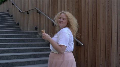 A Plump Caucasian Woman Eats An Ice Cream Cone While Walking Stock