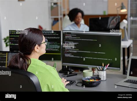 Rear View Of Female Brunette Senior It Specialist Coding Database Script On Multiple Screens In Rear View Of Female Brunette Senior It Specialist Coding Database Script On Multiple Screens In