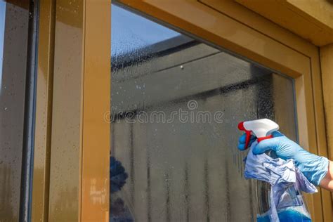 View Of A Woman Spraying Window Cleaning Spray On An Outdoor Window