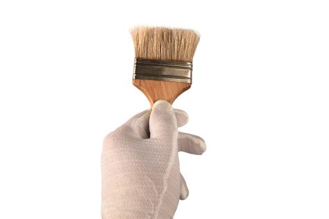 흰색 장갑에 손을 브러시를 수납 흰색 배경에 격리 된 클로즈업 그림 장식 주택 개조 또는 개조의 개념 염색을 위한 작업 도구로서 페인트 브러시 Diy에 대한 스톡 사진 및