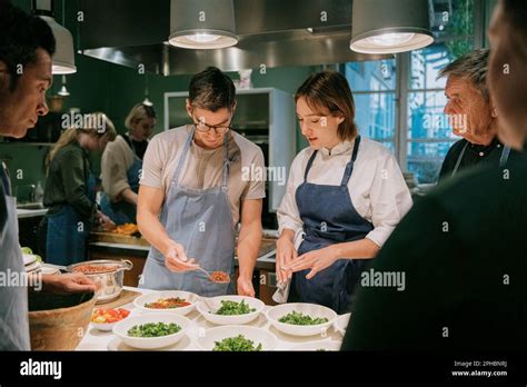 Female Chef Assisting Male Student During Cooking Class In Kitchen