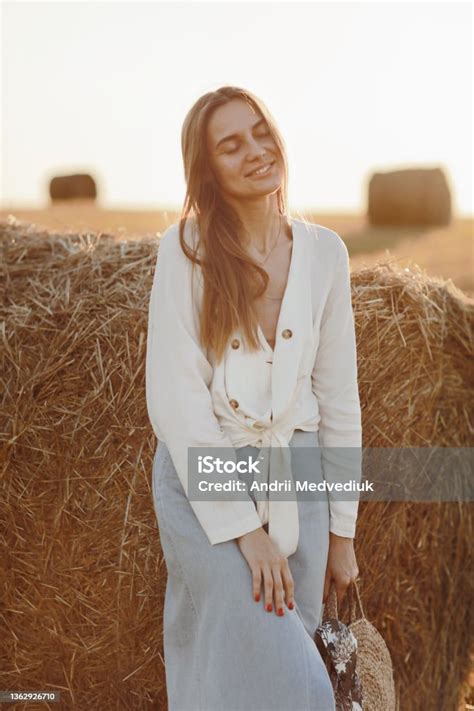 청바지 스커트와 손에 밀짚 가방에 미소 아름다운 갈색 머리의 전체 길이 초상화 여름 화창한 날에 건초 베일이 있는 밀밭에서