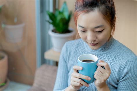 따뜻한 커피 한 잔과 함께 조용한 순간을 즐기고 부드러운 자연 채광과 식물이 있는 아늑한 실내 환경에서 평화롭게 아래를 내려다보는 젊은 아시아 여성 가을에 대한 스톡 사진