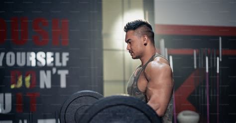 강한 젊은 운동 선수는 피트니스 체육관에서 바벨 무게를 들어 올리는 남자에 적합합니다 몸에서 근육질의 힘을 보여주는 운동복을