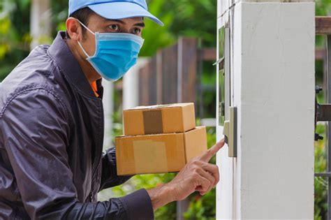 배달 남자는 위생 마스크와 파란색 모자를 착용 종과 고객의 집 앞에서 골판지 상자를 들고 배달부에 대한 스톡 사진 및 기타
