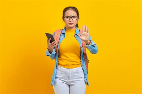 배낭을 들고 노란 배경에 고립 된 정지 제스처를 보여주는 배낭으로 캐주얼 한 옷을 입은 젊은 아시아 여성 학생의 초상화 모던 양식에 대한 스톡 사진 및 기타 이미지 Istock