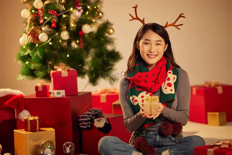 아름다운 여인이 크리스마스 트리 앞에 앉아 손에 선물을 들고 있다 사진 무료 다운로드 Lovepik