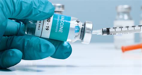 투명한 액체 코로나바이러스 백신 병과 실험실에서 주사를 위한 주사기가 있는 파란 의학 장갑을 입은 여성 의사의 손을 클로즈업합니다 질병에 대한 새로운 치료법의 연구 및 개발