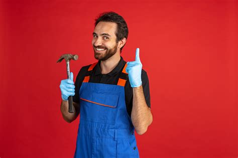 재미있는 젊은 수염 남자 남성 자동차 정비사 또는 파란색 작업 Dungarees 빨간 스튜디오 배경에 고립 된 옷을 입고 피터 얼굴 감정의 개념 밈에 대한 스톡 사진 및