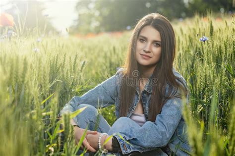 Beautiful Brunette Girl Dressed In Jeans Is Sitting In Cornyfield Stock