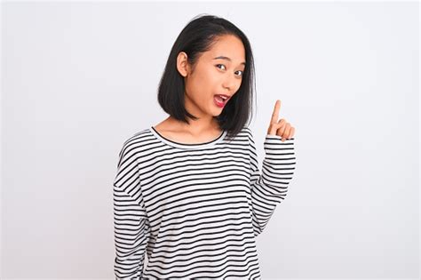 스트라이프 티셔츠를 입은 젊은 중국 여성이 성공적인 아이디어로 손가락을 가리키는 고립 된 흰색 배경 위에 서 있습니다 종료하고 행복 넘버 원 T 셔츠에 대한 스톡 사진 및