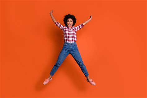 전신 사진 흥분 미친 점프 높은 여자 고함 예 손을 제기 손을 착용 청바지 데님 바지 격자 무늬 셔츠 의상 고립 된 오렌지 배경 갈색 머리에 대한 스톡 사진 및 기타 이미지