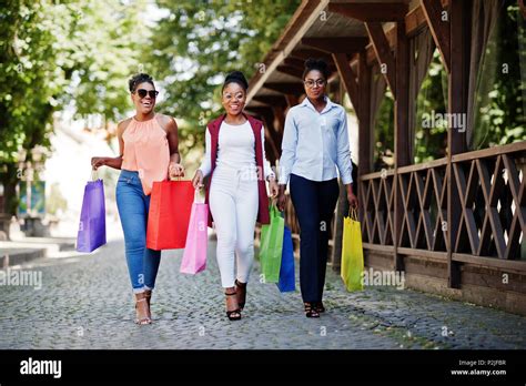 Three Casual African American Girls With Colored Shopping Bags Walking