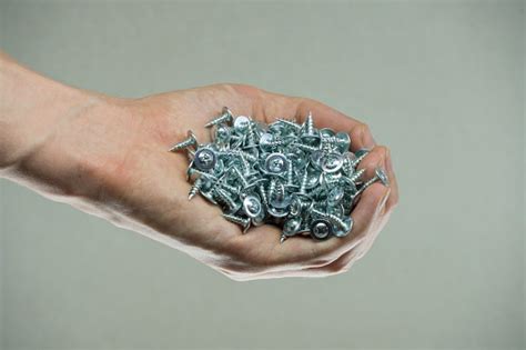 남자의 손에 볼트 나사와 톱니바퀴 고정 및 수리를 위한 도구입니다 스테인레스 스틸 볼트 아연 도금 금속 패스너 금속 나사 더미가