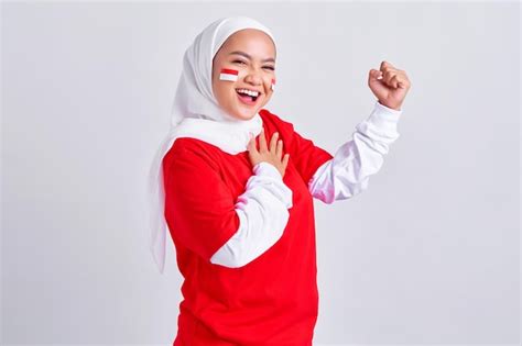 흰색 배경에 격리된 8월 17일 인도네시아 독립 기념일을 축하하는 빨간색 흰색 티셔츠를 입은 흥분한 젊은 아시아 이슬람 여성 프리미엄 사진