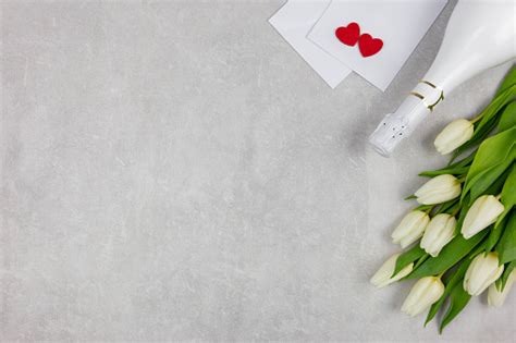 밝은 회색 콘크리트 배경에 샴페인 봉투와 붉은 하트와 흰색 튤립 꽃 발렌타인 여성 어머니의 날 부활절 생일 또는 결혼식 휴일 플랫 평지 맨 위 보기입니다 공간을 복사합니다