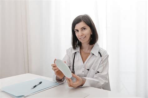 식탁에 앉아 있는 동안 깔창을 들고 있는 의사 정형 외과 의사는 의료 기기를 테스트합니다 정형 외과 깔창 발 관리 플랫 피트 보정 평평한 발 및 발 질환의 치료 및 예방