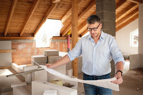 안경과 파란색 셔츠를 입은 남성 건축가가 다락방 의 건설 현장에서 건축 계획을 검토합니다 남자들만에 대한 스톡 사진 및 기타 이미지 남자들만 백인종 40 44세