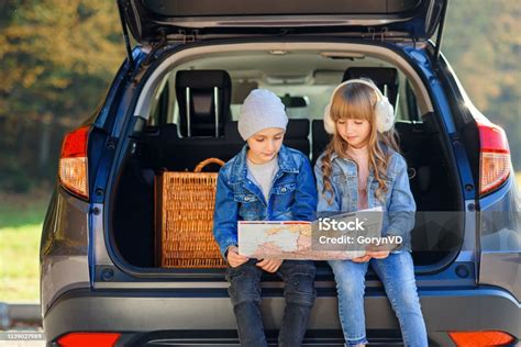 귀여운 세련된 소년과 예쁜 10s 소녀는 자동차의 트렁크에 앉아서 가족 여행에 올바른 방향을 논의하는 동안 도로지도를보고 자동차로 가족 휴가 여행 10 11세에 대한 스톡