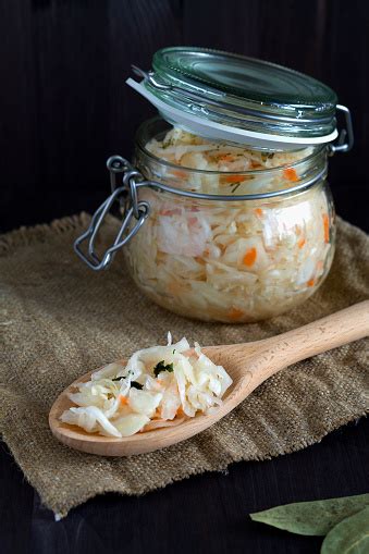 검은 색 배경에 유리 항아리에 허브와 당근과 수제 소금에 절인 양배추 나무 테이블에 자루천이 있는 숟가락에 양배추를 절인 양배추 통조림 식품의 개념 복사 공간을 복사합니다