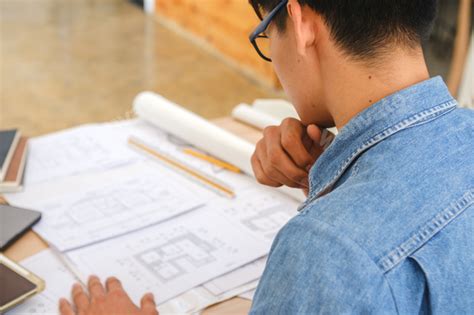 Architect And Engineer Analyzing Blueprints At A Work Desk In An Office