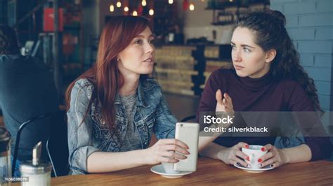 두 매력적인 여성 캐주얼 옷에 얘기 하 고 커피 컵 및 스마트폰 카페에 여자 시간을 보내고 있다 좋은 카페 인테리어 고객 및 가구를 볼 수 있습니다 2명에 대한 스톡 사진