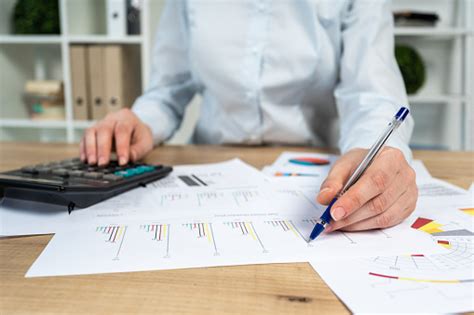 그녀 뒤에 앉아 테이블 차트 그래프 다이어그램 그래픽에 밝은 로프트 인테리어 마크 중요 한 자리에와 펜 포커스로 손에 그녀의 Formalwear에 여자의 사진 가까이 잘리지