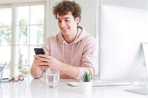 행복 한 얼굴이 있는 스마트 폰과 컴퓨터를 사용 하 여 젊은 학생 남자는 치아를 보여주는 자신감 미소와 함께 웃 고 십대 소년에