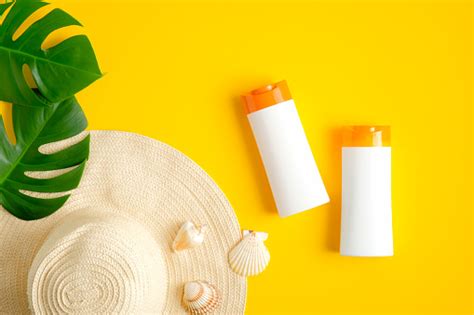 노란색 배경에 라벨 열대 잎과 해변 모자없이 선스크린 크림과 로션 병 모형 상단보기 평평한 누워 자외선 차단 및 여름 스킨케어