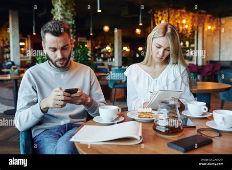 serious guy scrolling in smartphone while his girlfriend making notes