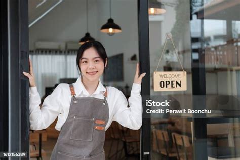 그녀의 카페 앞에 열린 간판이 있는 아름답고 웃는 바리스타 아름다운 미소로 그녀의 가게에서 고객을 맞이합니다 Home Front