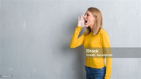 그런 지 회색 벽 소리 고 크게 입에 손으로 측면에 서 있는 아름 다운 젊은 여자 통신 개념입니다 비명에 대한 스톡 사진 및 기타 이미지 Istock