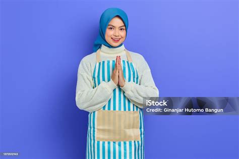 히잡과 앞치마를 입은 쾌활한 젊은 아시아 무슬림 여성 보라색 배경에 고립 된 고객을 맞이하고 인사하는 열린 표지판 사람들 주부