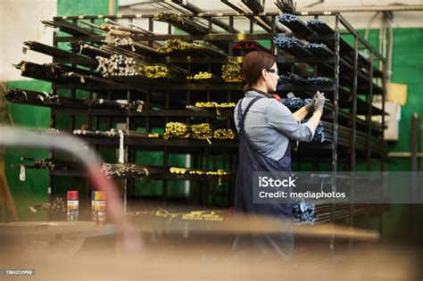 화려한 막대기로 금속 선반에 서서 공장에서 분류하는 바지에 여성 창고 노동자의 뒷모습 공장 산업 건물에 대한 스톡 사진 및 기타