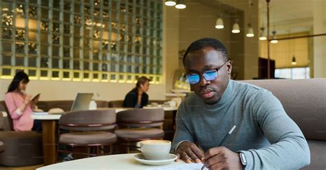 젊은 아프리카 사업가가 커피를 마시며 테이블에 앉아 문서에 메모를 하고 카페에서 커피 브레이크 시간에 일하고 있습니다 사진 Unsplash의 카페 이미지