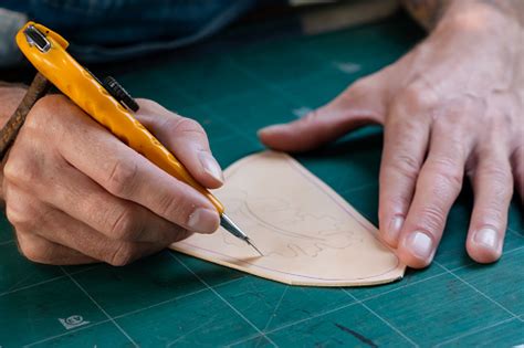 소의 피부에 커터 슬릿을 사용하는 클로즈업 손 신발을 만드는 데 사용하기 위해 가죽의 패터닝을 위한 또 다른 단계이며 장인은 손으로 소가죽을 꼼꼼하게 자르고 있습니다 40