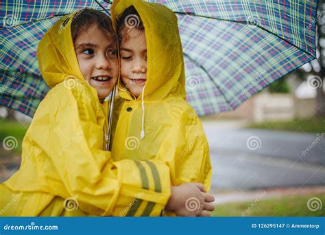 Прелестные девушки в плащах обнимая один другого под зонтиком Стоковое Изображение изображение