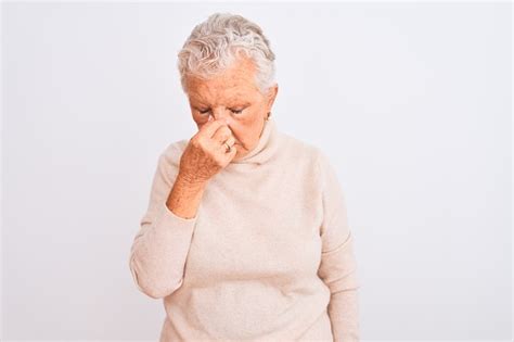 고립 된 흰색 배경 에 서 터틀넥 스웨터를 입고 선임 회색 머리 여자는 피로와 두통을 느끼는 코와 눈을 문질러 피곤 스트레스와