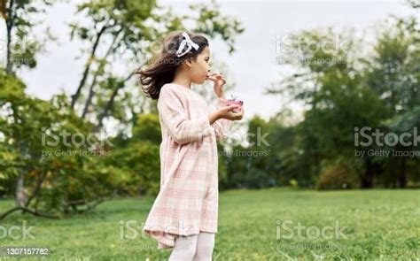 분홍색 드레스를 입은 어린 소녀가 공원에서 손에 생일 컵케이크를 맛보습니다 행복한 귀여운 아이가 야외에서 생일을 축하합니다 6 7 살에 대한 스톡 사진 및 기타 이미지